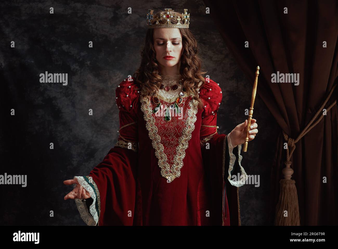 medieval queen in red dress with wand and crown on dark gray background ...