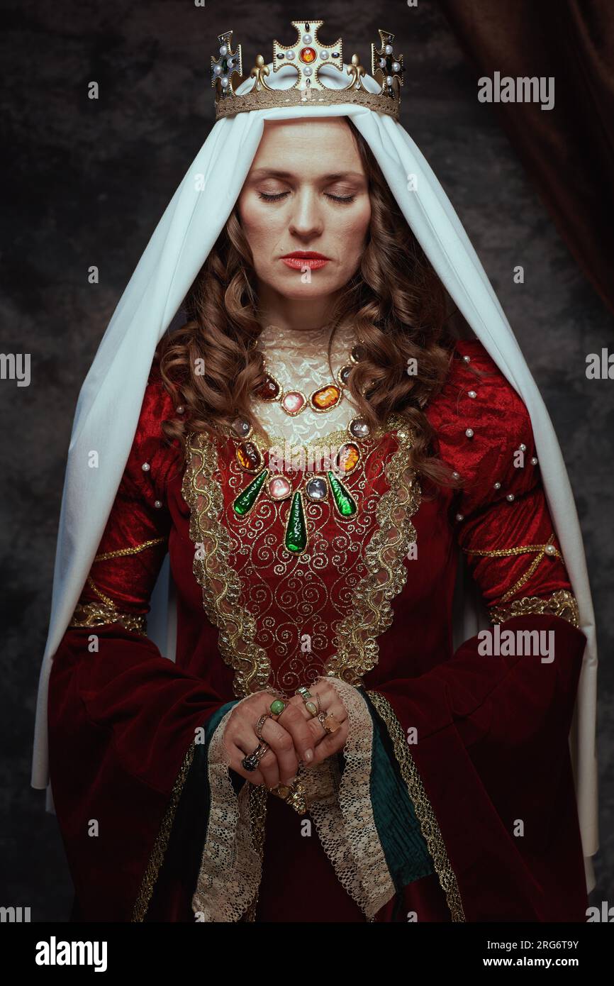 medieval queen in red dress with veil and crown on dark gray background ...