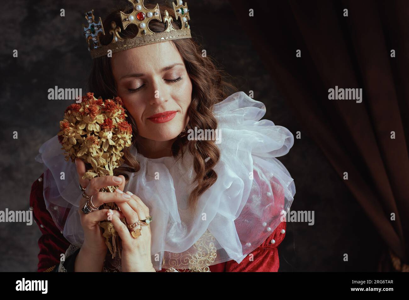 relaxed medieval queen in red dress with dried flower, white collar and ...