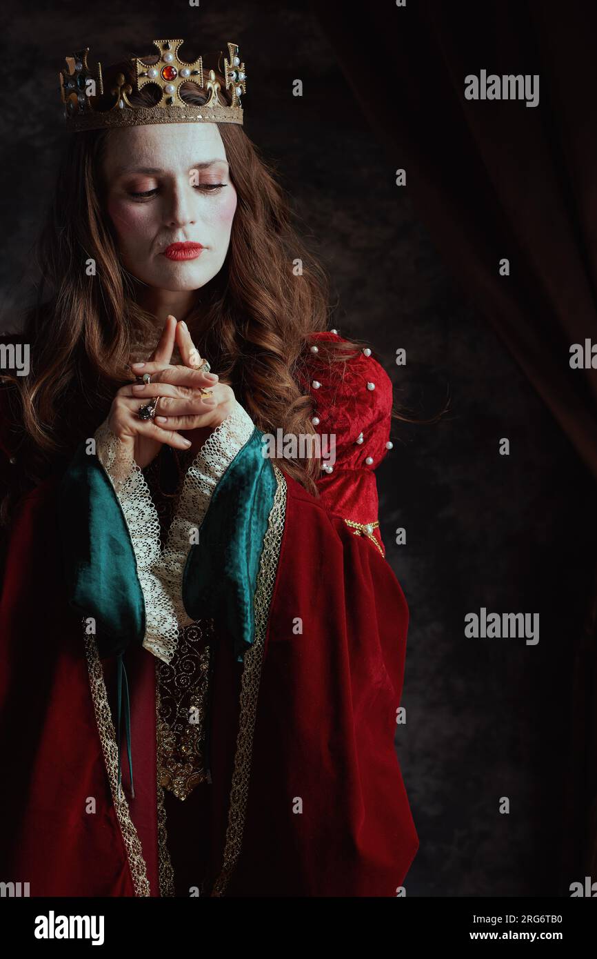 medieval queen in red dress with white makeup and crown on dark gray ...