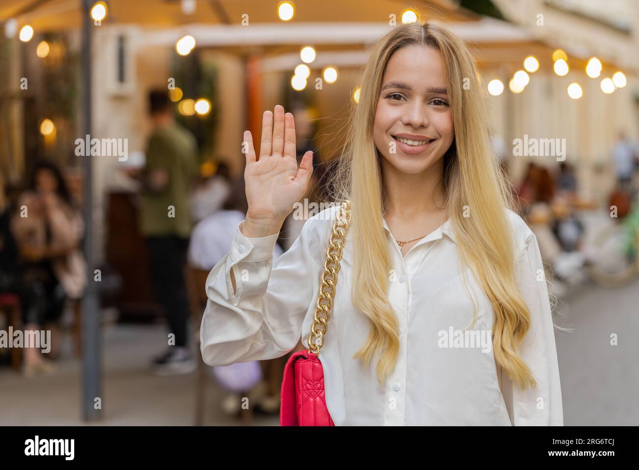 Blonde young woman smiling friendly at camera, waving hands gesturing ...