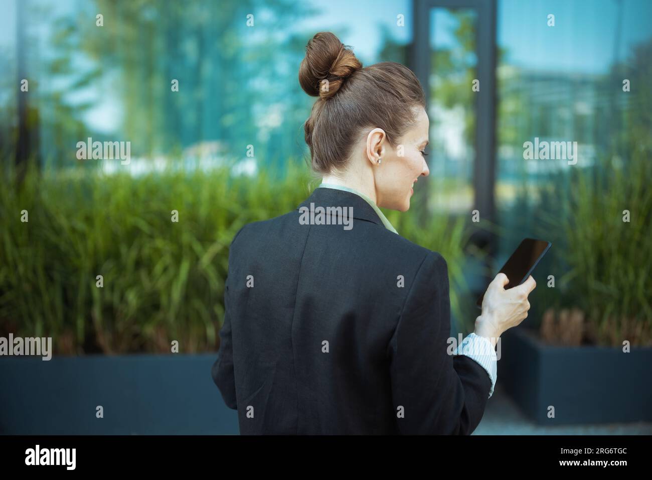 Seen from behind woman employee near office building in black jacket ...