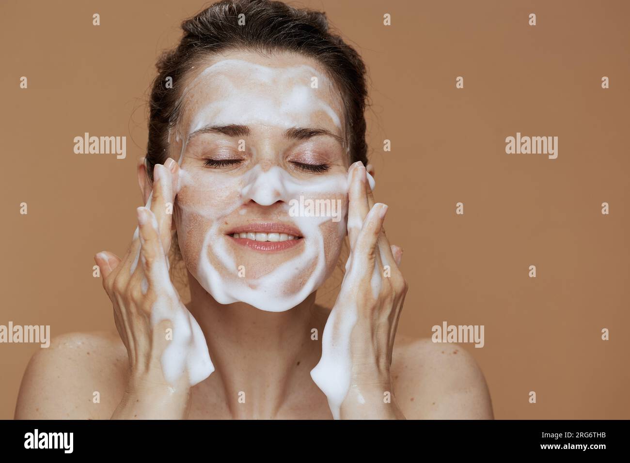 happy young female with foaming face wash washing face on beige ...