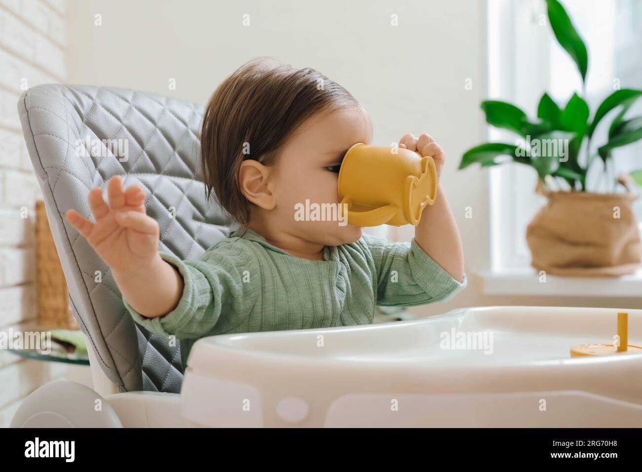 Cute little baby drinking from cup in high chair indoors Stock Photo ...