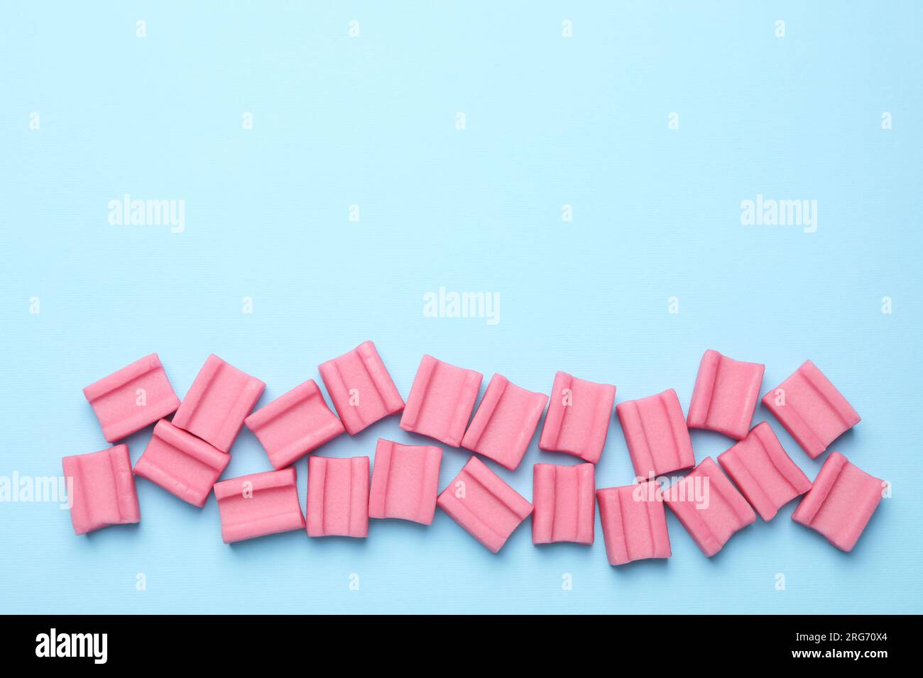 Tasty pink chewing gums on light blue background, flat lay. Space for ...