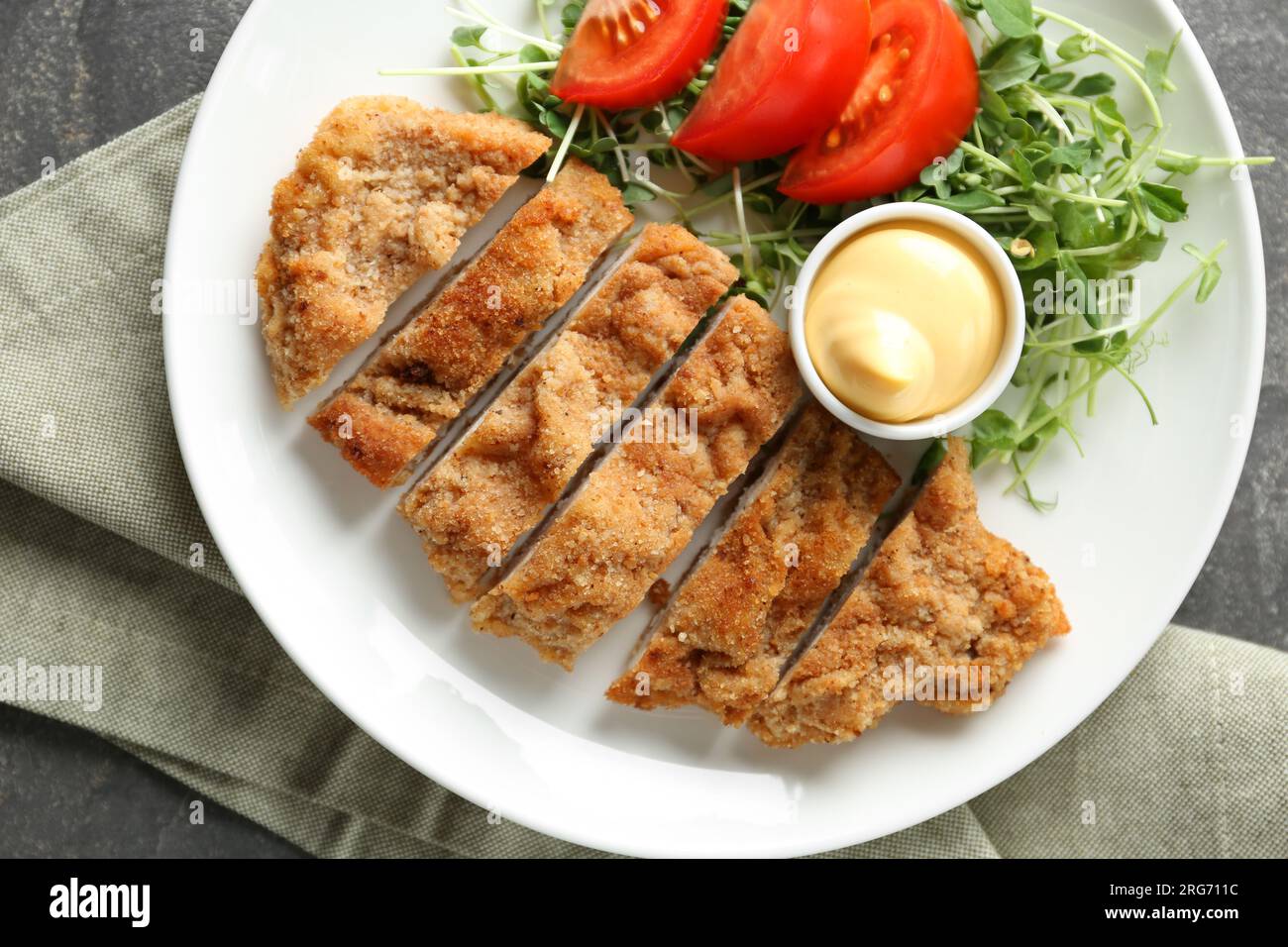 Tasty cut schnitzel served with sauce, microgreens and tomato on grey ...