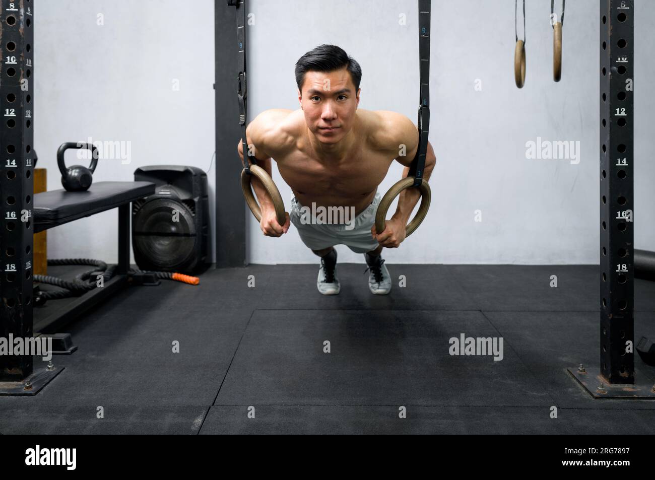 Athlete performing intense pull-up workout on gymnastic rings in a well ...