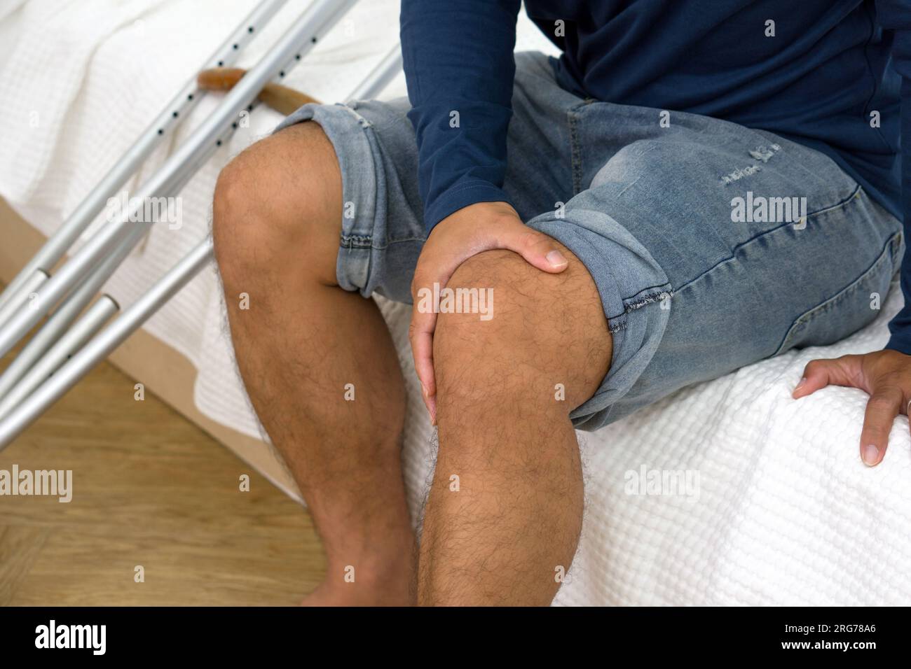 Injured man with painful knee resting on bed in an indoor setting ...