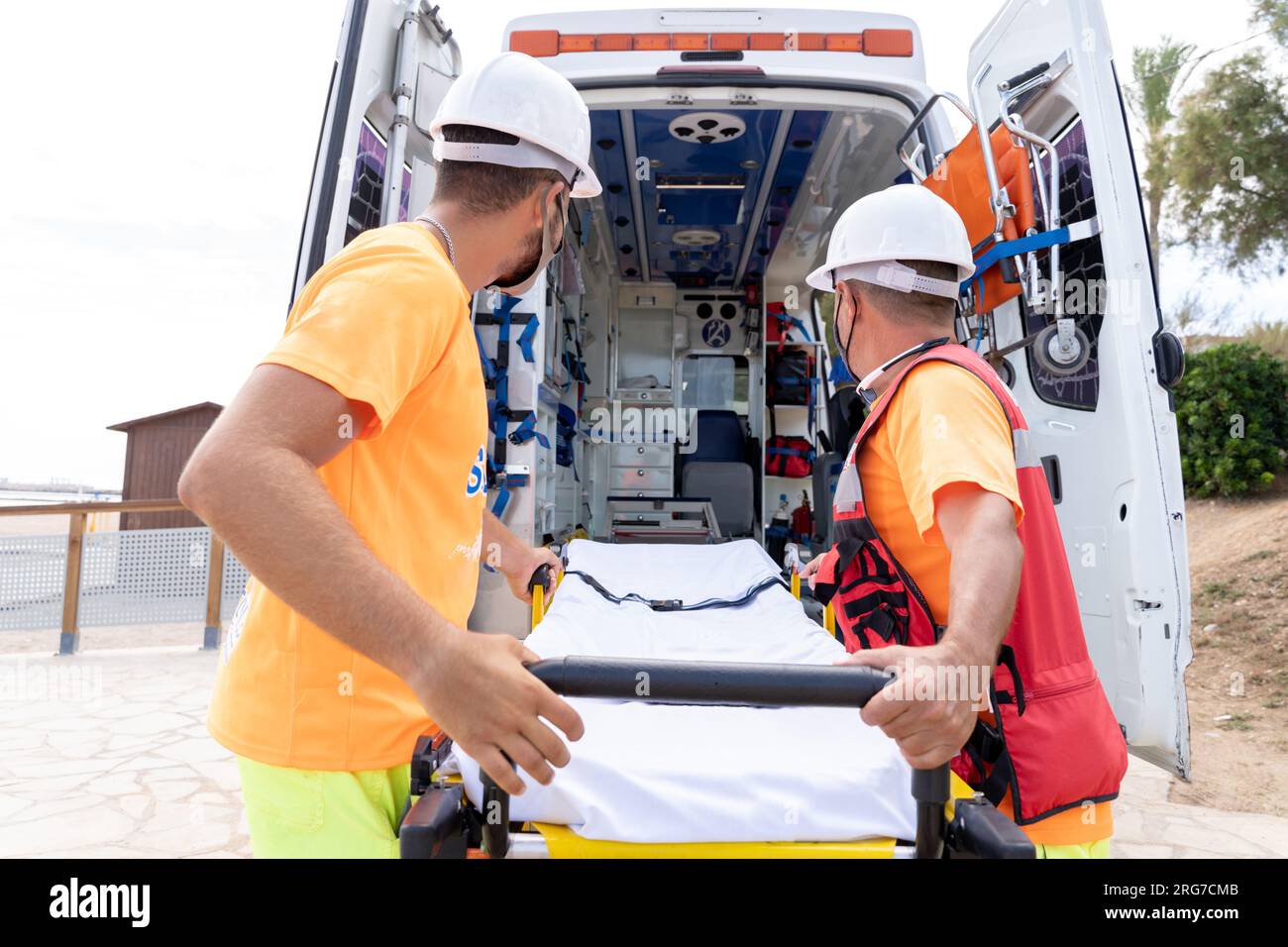 Rear view of two lifeguards taking a stretcher out of ambulance on the ...