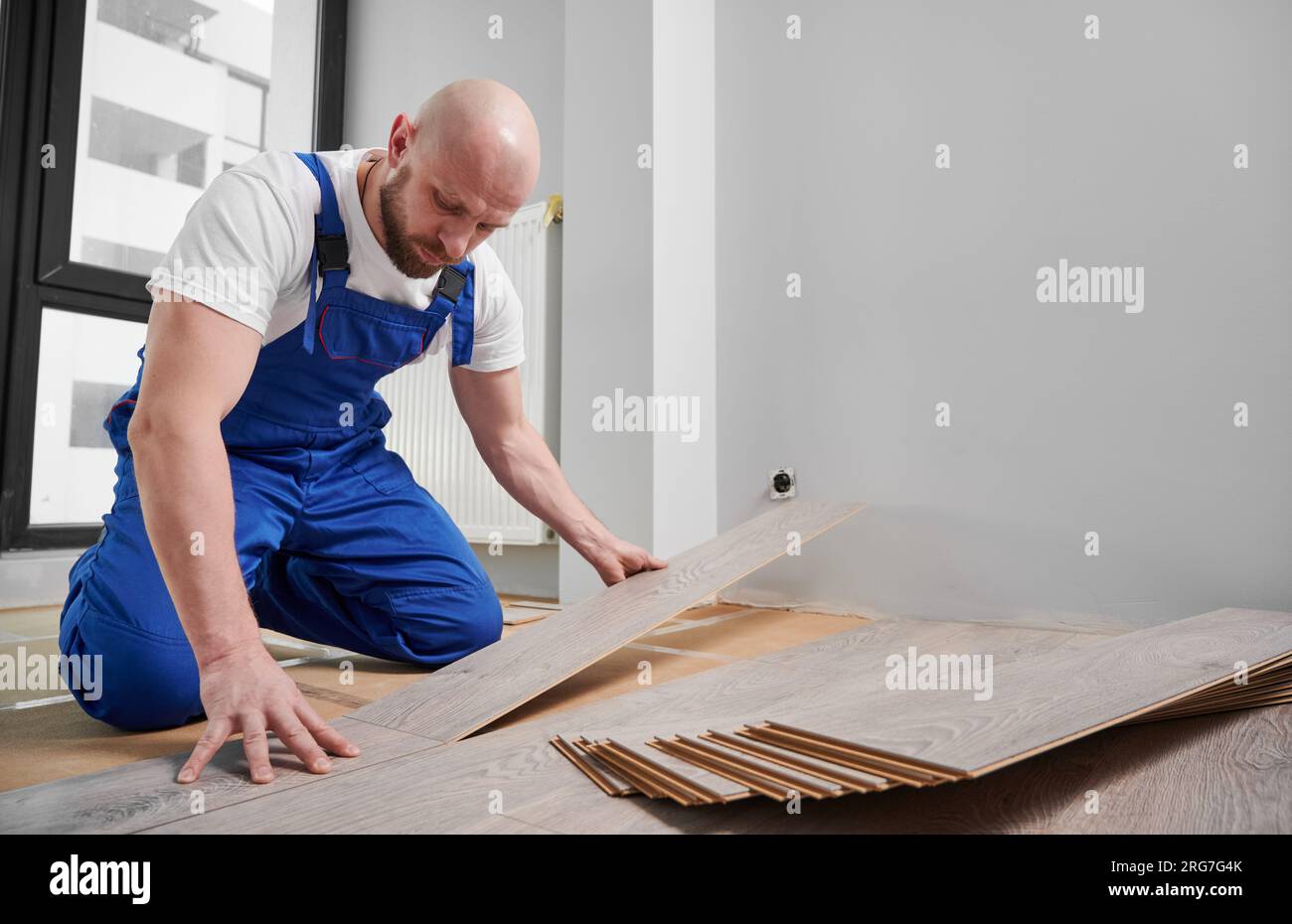 Male construction worker laying laminate wood plank on floor ...