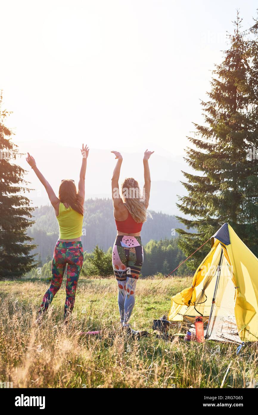 Two women tourists camping outdoors. Back view of young females friends traveling in hills ...