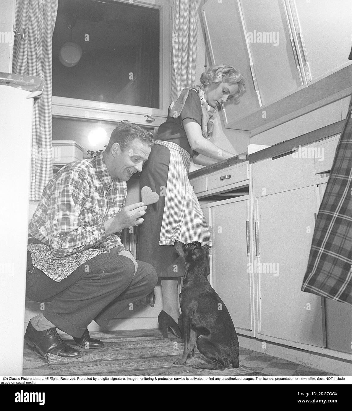 In the kitchen in the 1950s. Ayoung couple is seen baking heart shaped ...