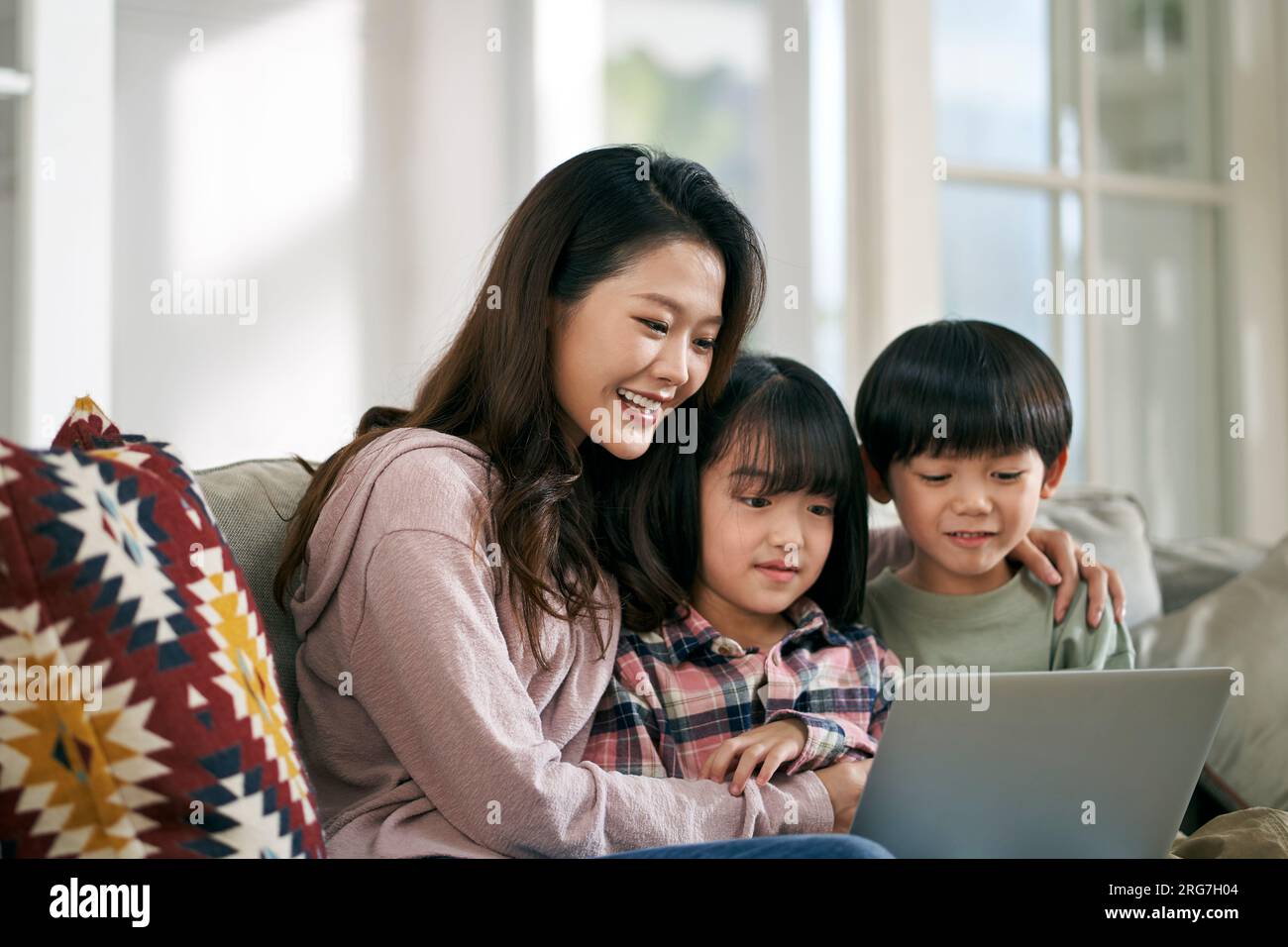 young asian mother and two children sitting on family couch at home ...