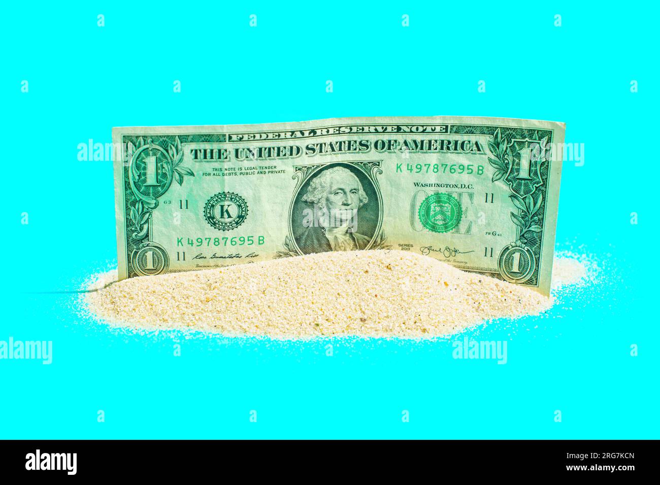 Single one-dollar bill is carefully placed on a mound of white sand ...