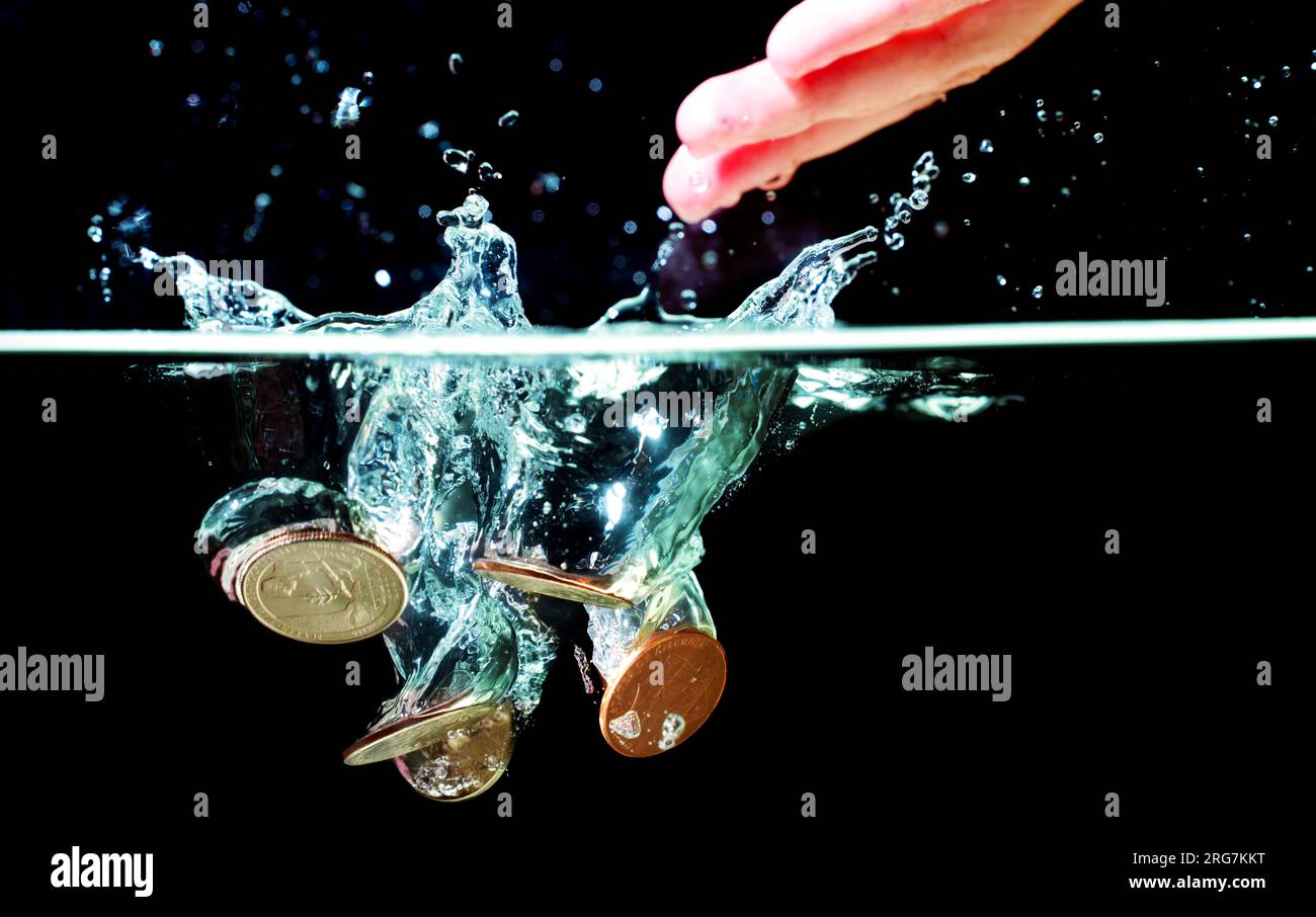 Hand drops some coins underwater with splashes on black Stock Photo - Alamy