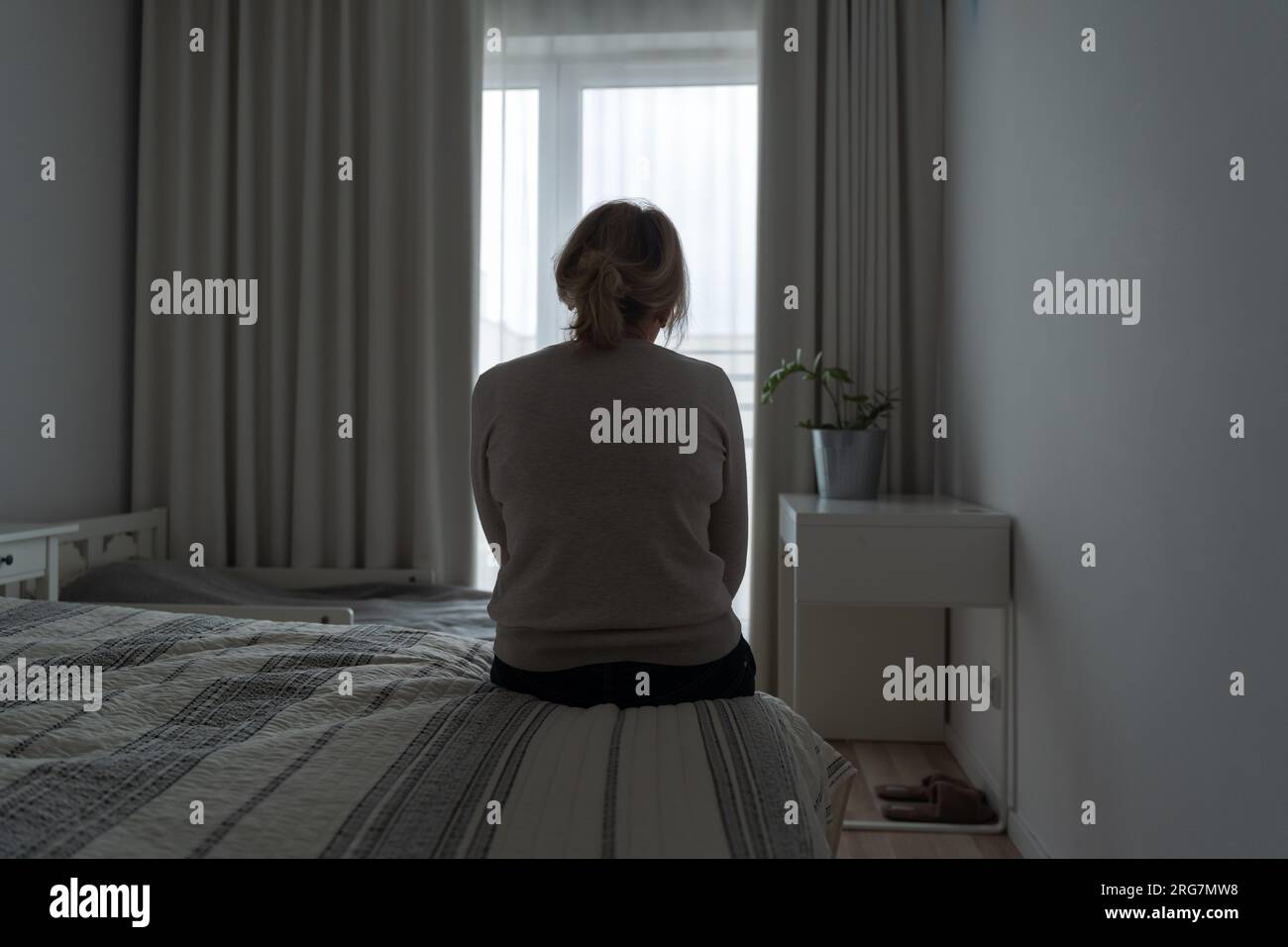 Mature woman sitting alone in the room, sad depressed person. Back view ...