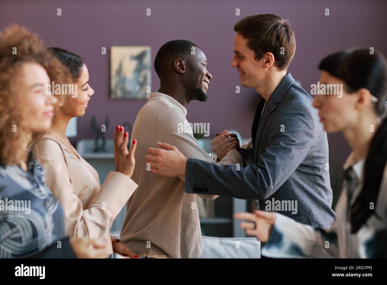 Two happy intercultural guys shaking hands and giving each other hug at ...