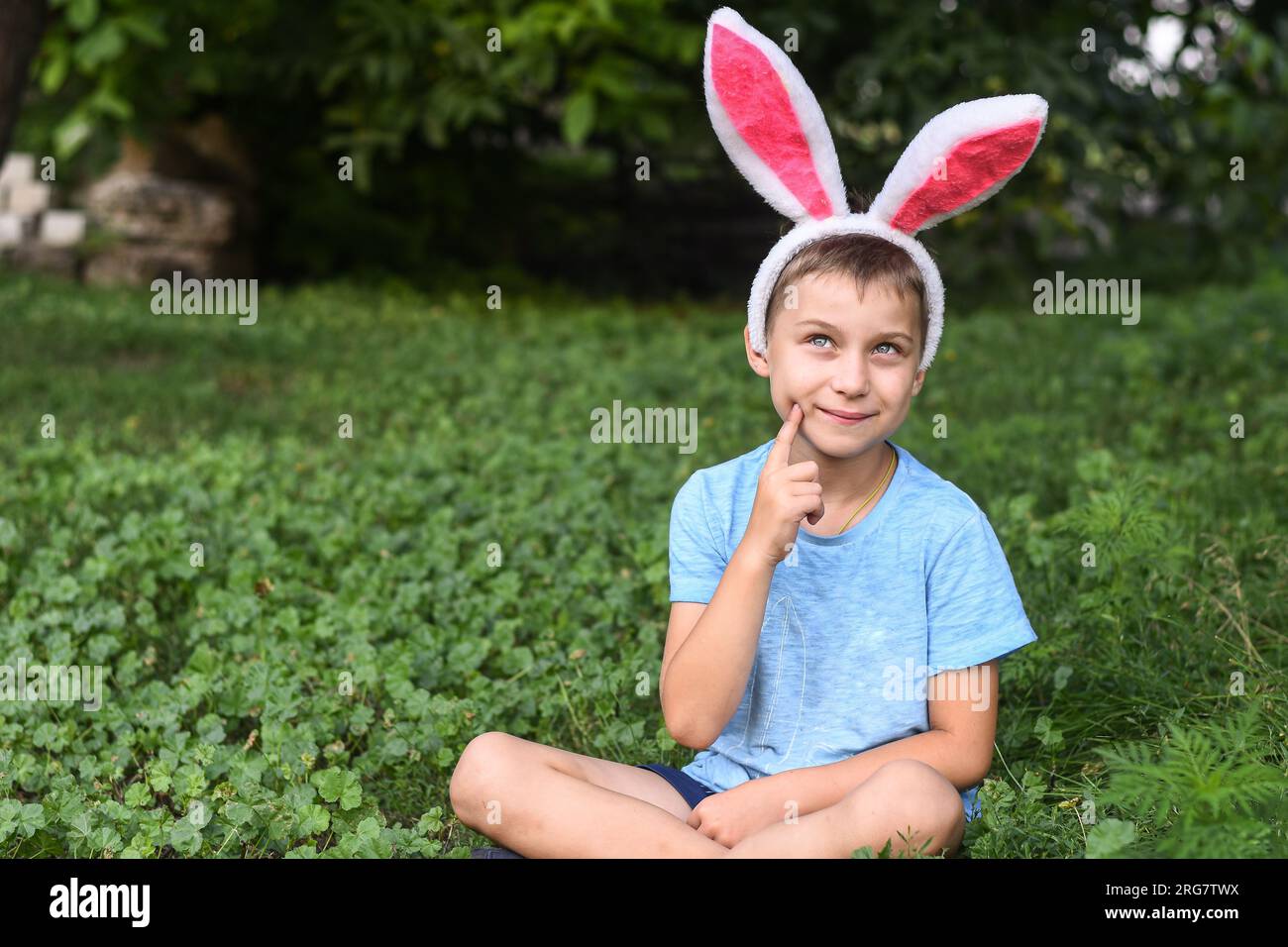 a thoughtful boy with the ears of a hare is sitting on the green grass ...