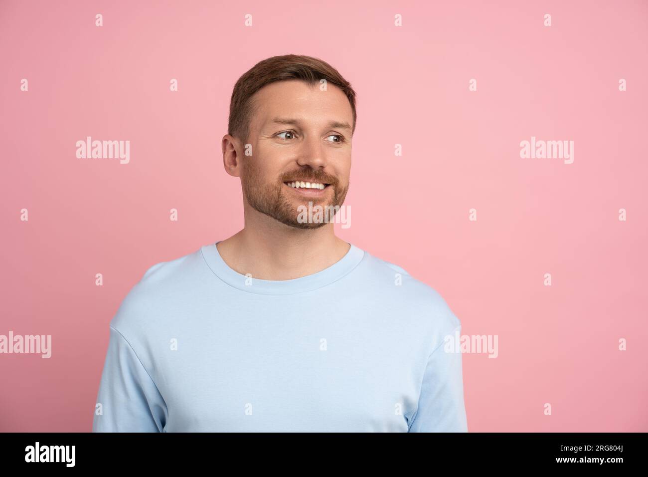 Smiling happy interested man looking to side on pink studio background ...