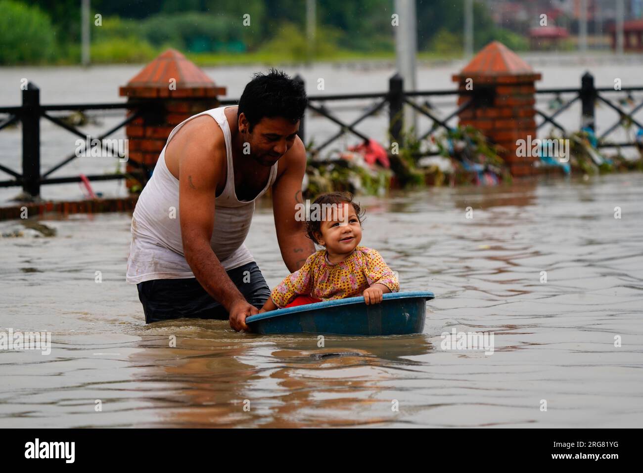 Kathmandu, Nepal. 08th Aug, 2023. A man takes his child outside their flooded home after heavy ...