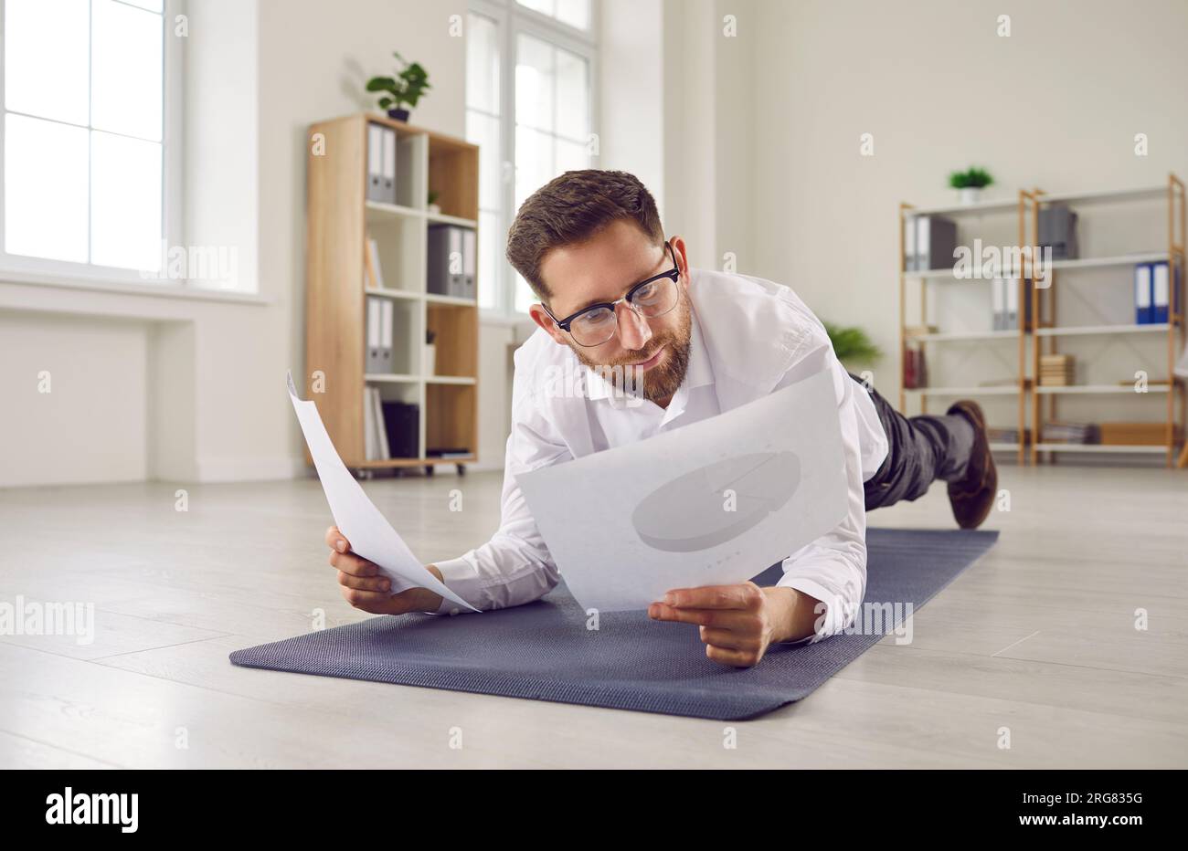 Funny man multitasking at work, reading business papers and doing ...