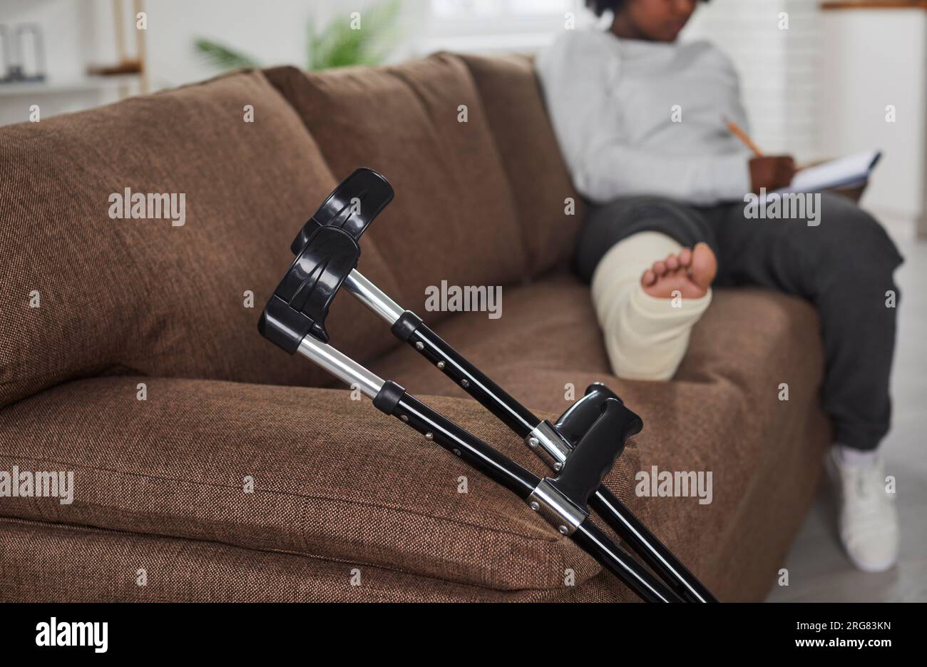 Crutches by sofa, with African American woman with broken leg resting ...