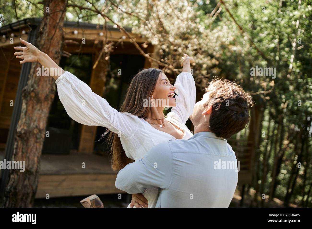 happy man lifting woman with outstretched hands, vacation house near ...