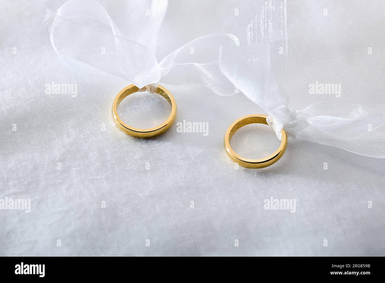 Detail of two gold wedding rings with white ribbon tied on white fabric ...