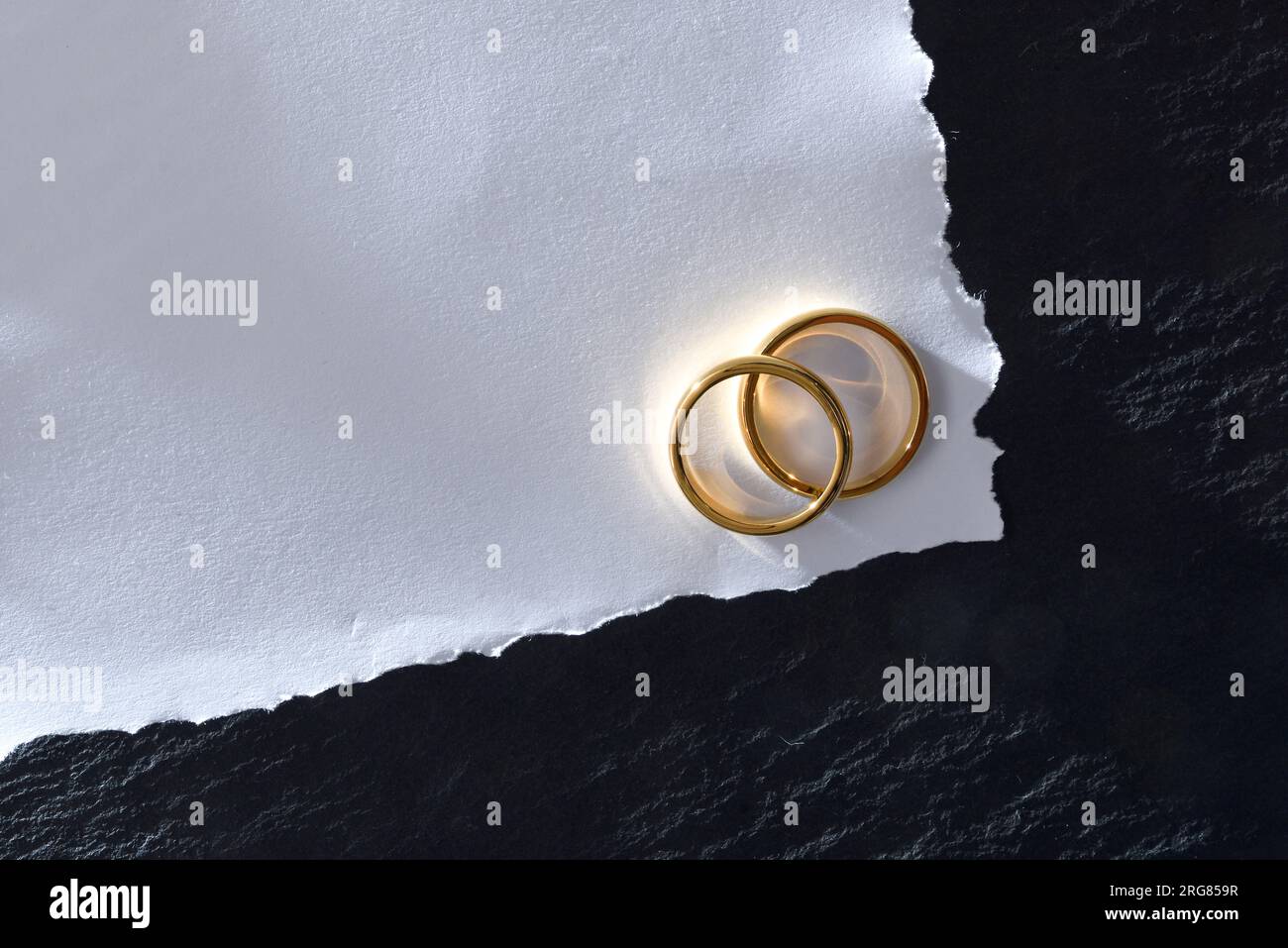 Macro of white textured paper card with two engagement rings on slate ...