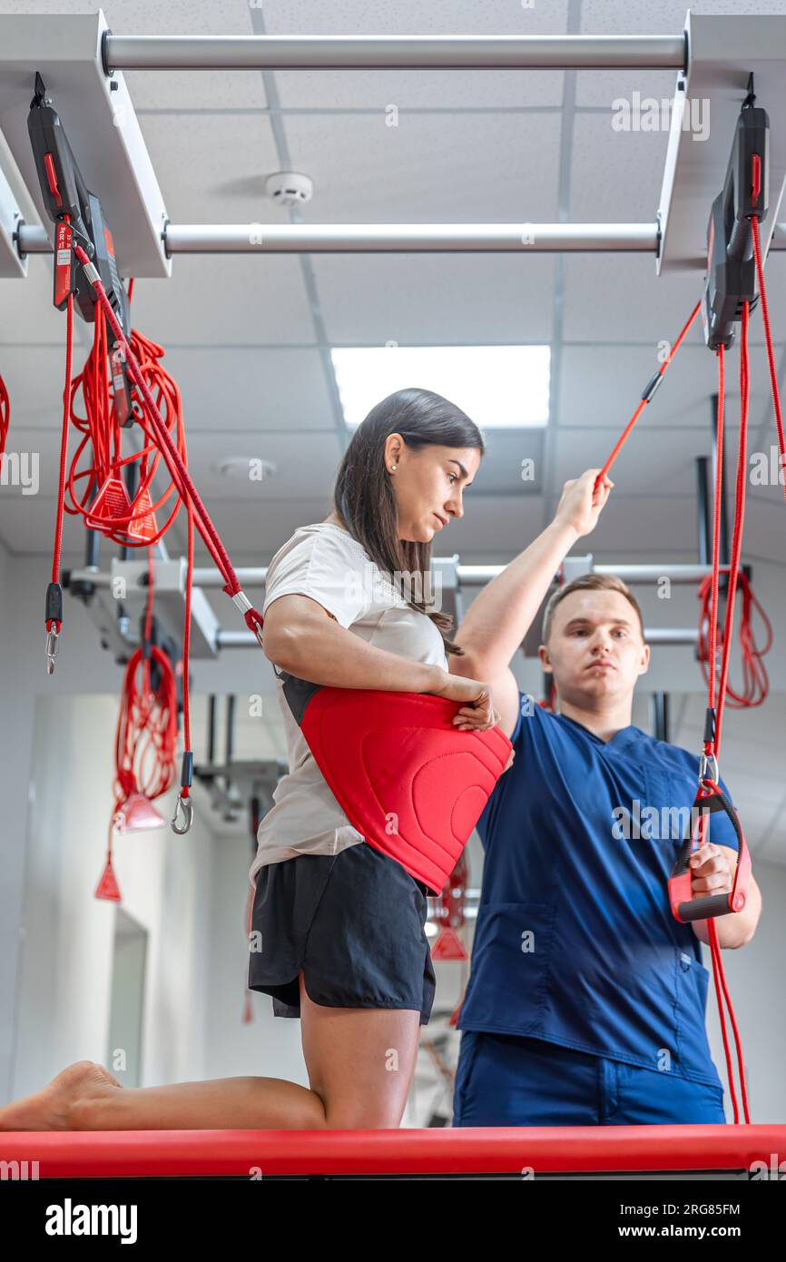 A young female is doing exercises with special ropes in rehabilitation ...
