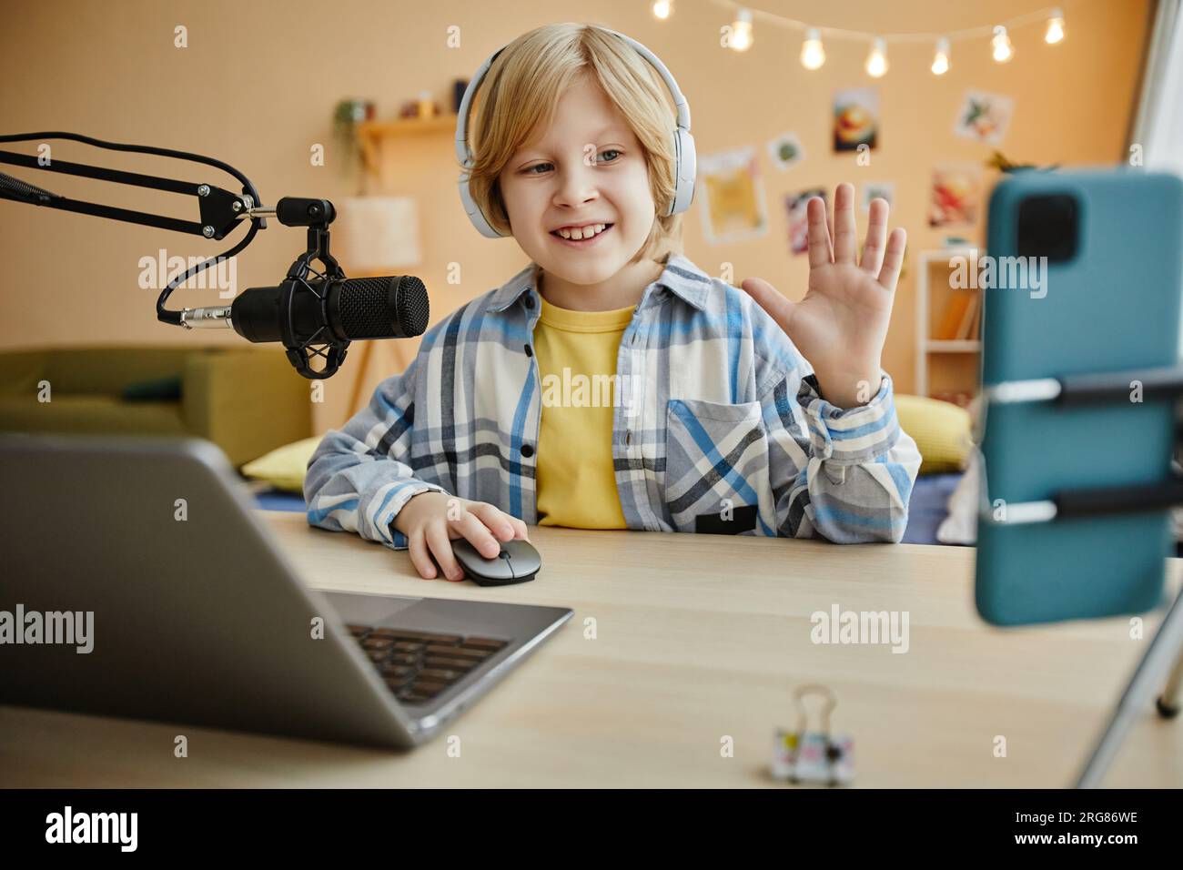 Smiling boy waving hand to online audience and speaking in microphone ...