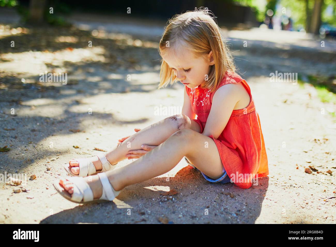 Cute little girl sitting on the ground after falling down. Child ...
