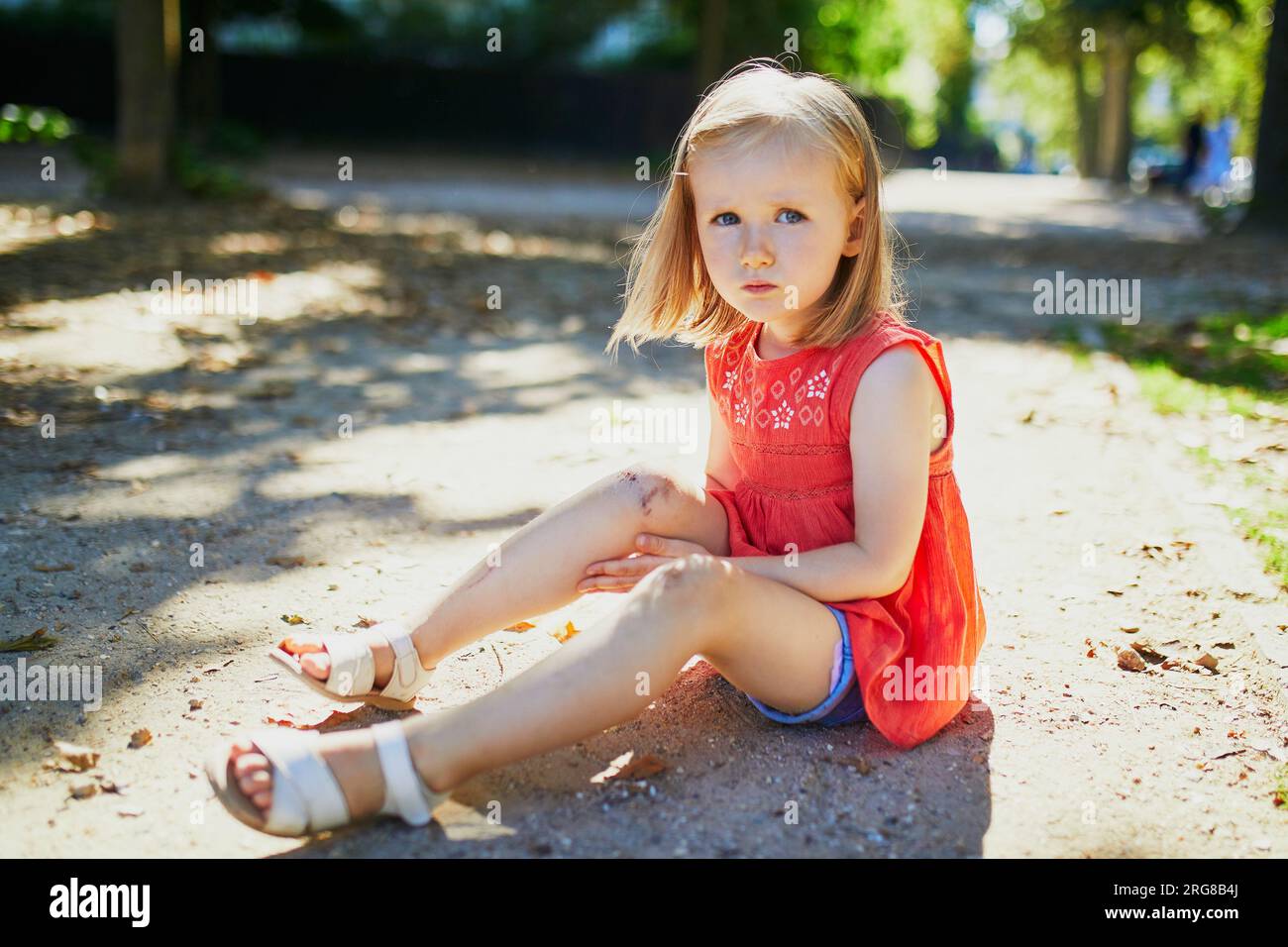 Cute little girl sitting on the ground after falling down. Child ...