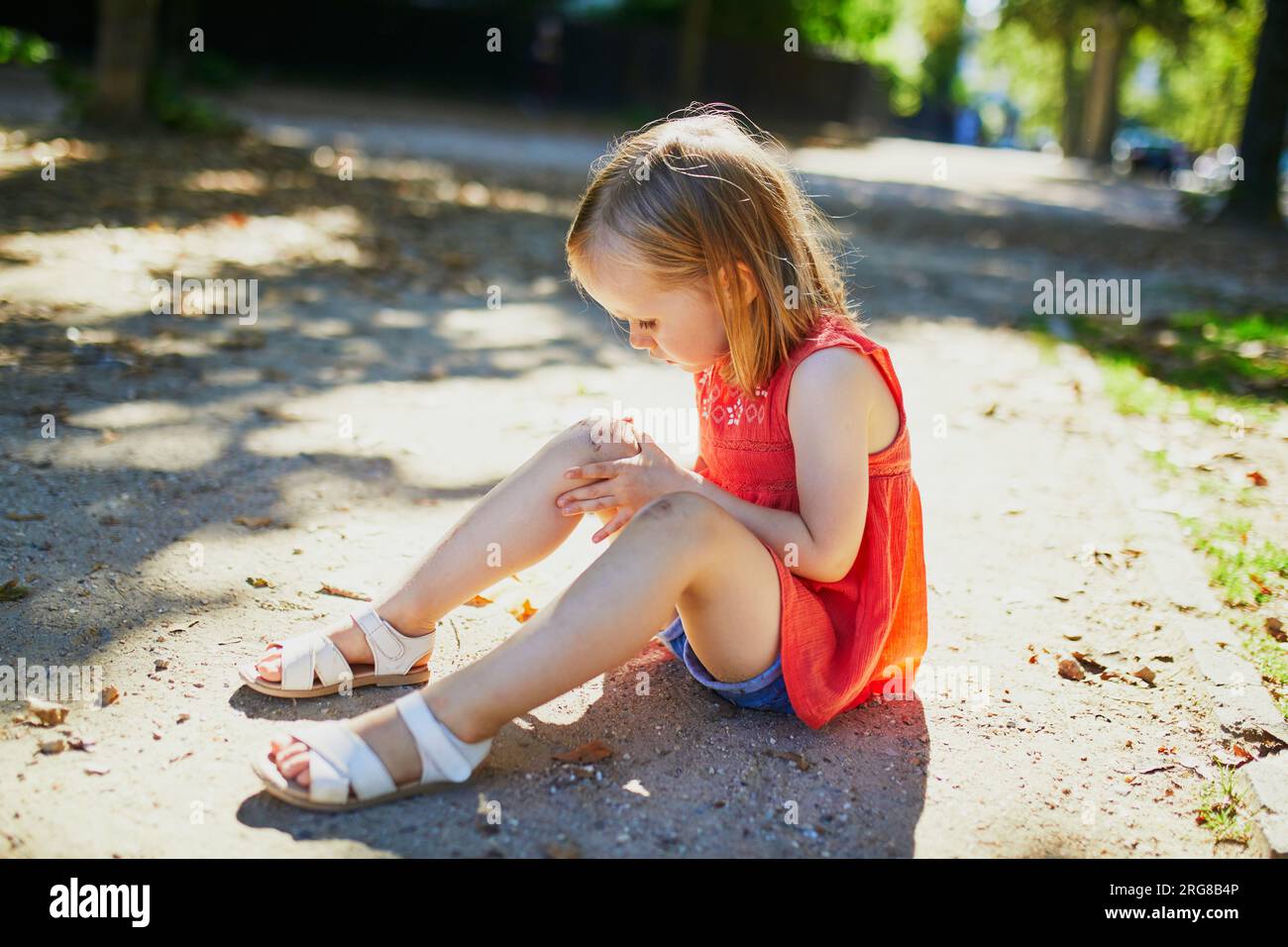 Cute little girl sitting on the ground after falling down. Child ...