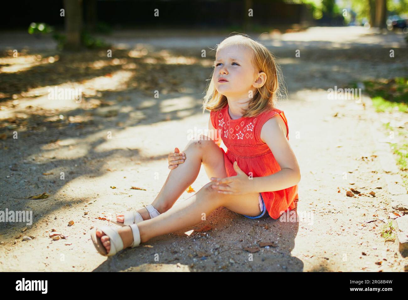 Cute little girl sitting on the ground after falling down. Child ...