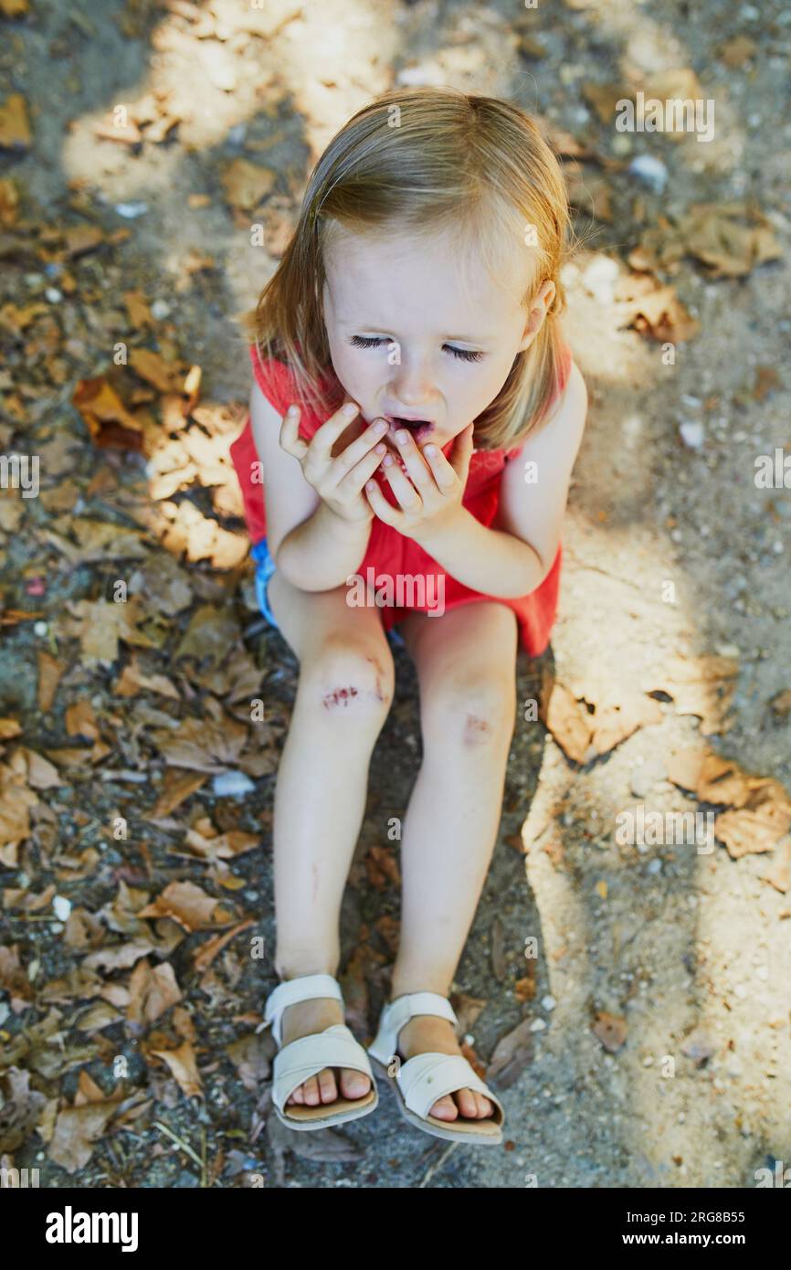 Cute little girl sitting on the ground after falling down. Child ...