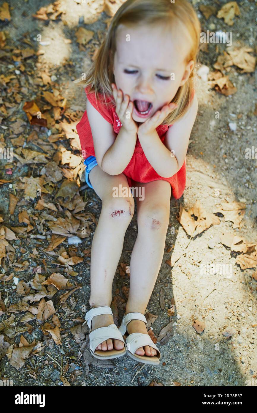 Cute little girl sitting on the ground after falling down. Child ...