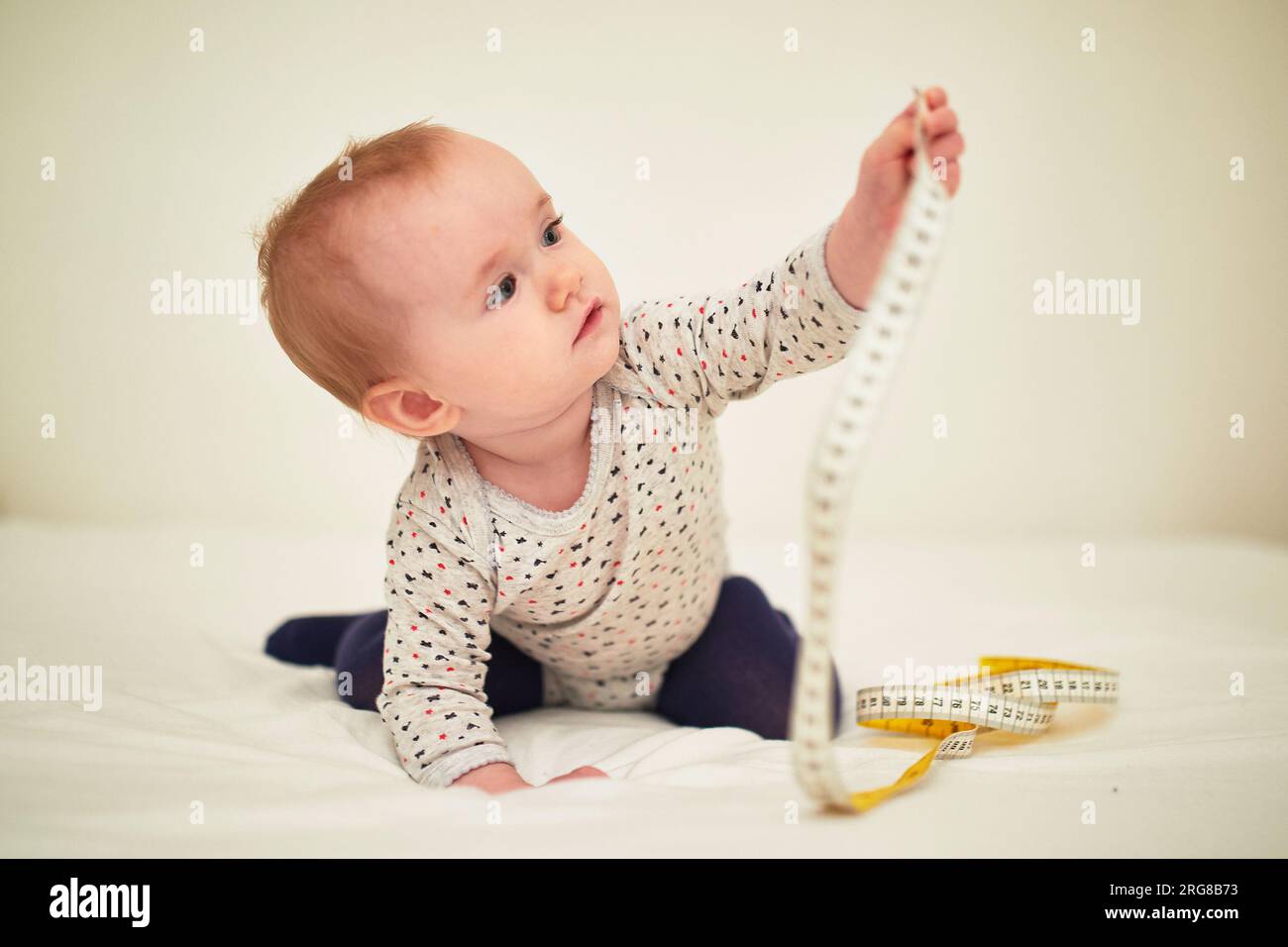 Cute little girl playing with centimeter tape measure on bed. Happy kid ...