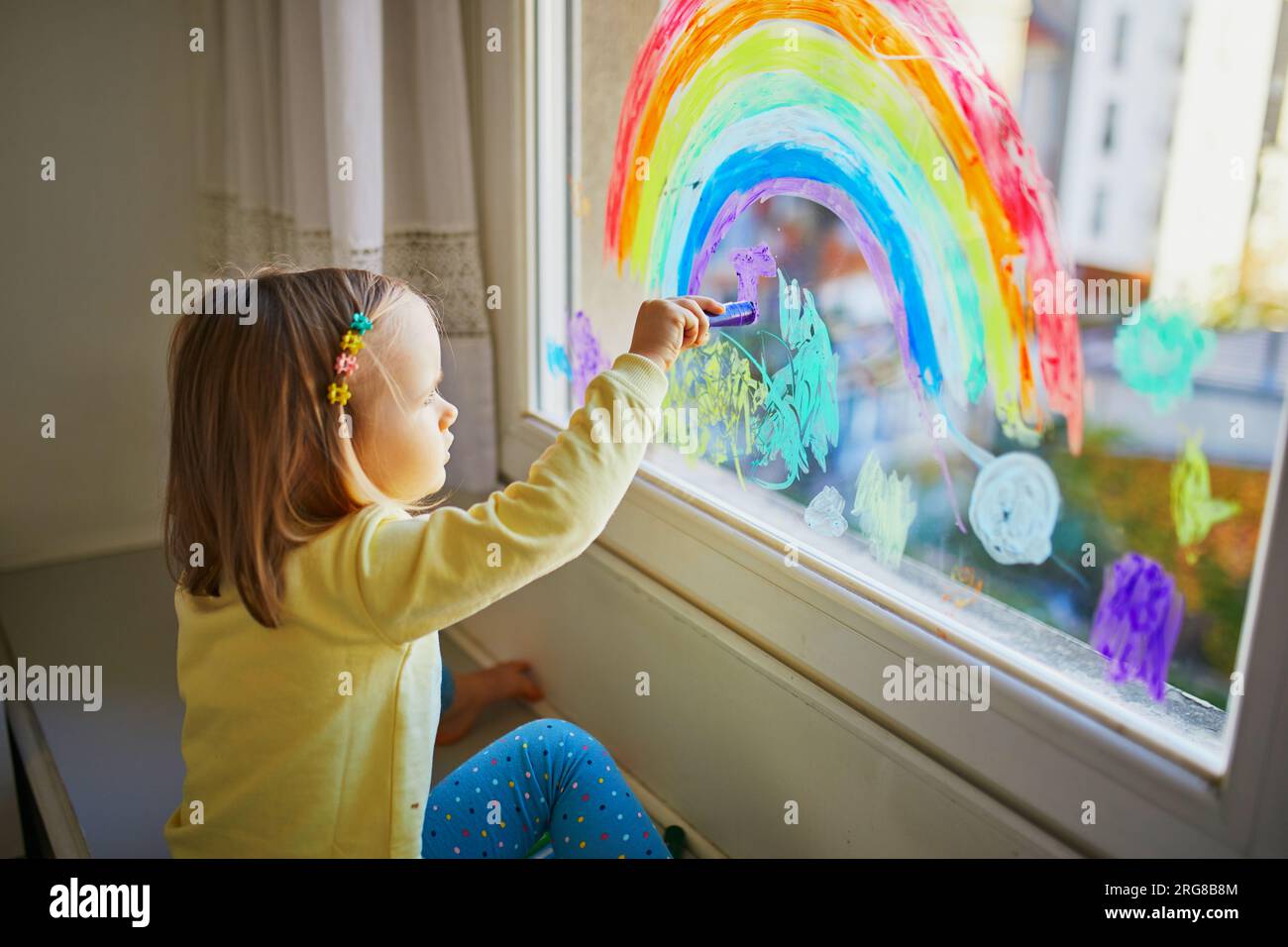 Adorable toddler girl drawing rainbow on window glass. Creative games ...