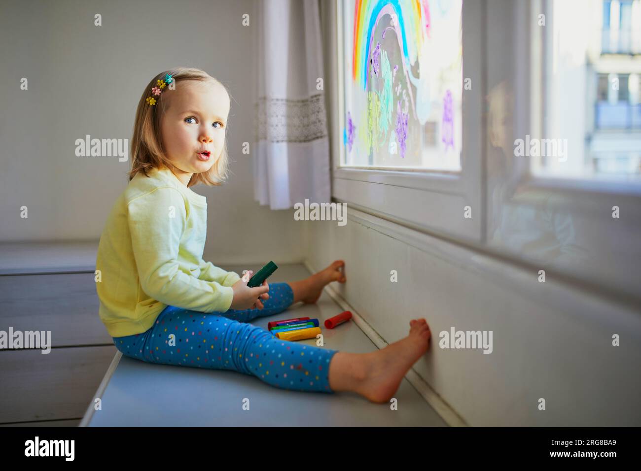 Adorable toddler girl drawing rainbow on window glass. Creative games ...