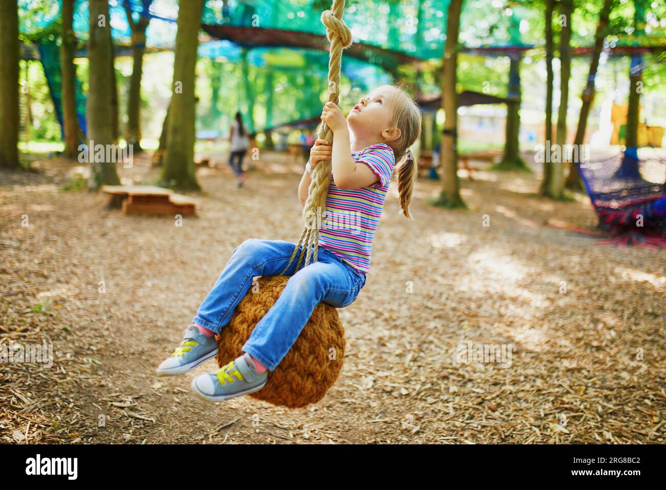 Adorable little girl having fun on rope swing in adventure park ...