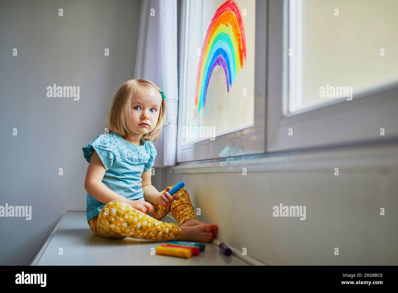 Adorable toddler girl drawing rainbow on window glass as sign of hope ...