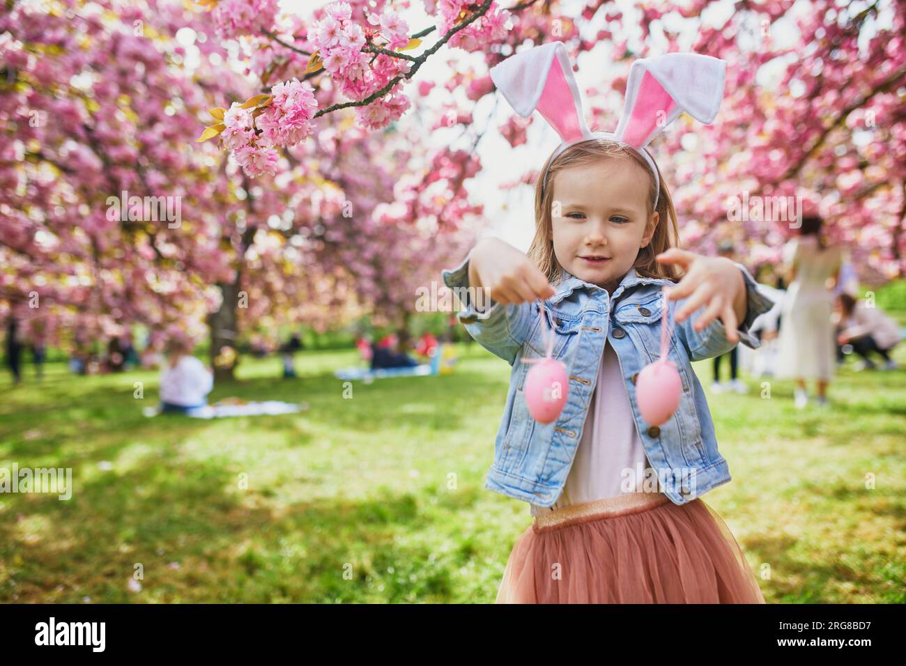 Preschooler girl wearing bunny ears playing egg hunt on Easter. Child ...
