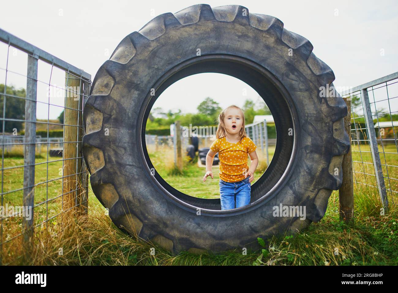 Adorable preschooler girl staying inside old tractor wheel on Gally ...