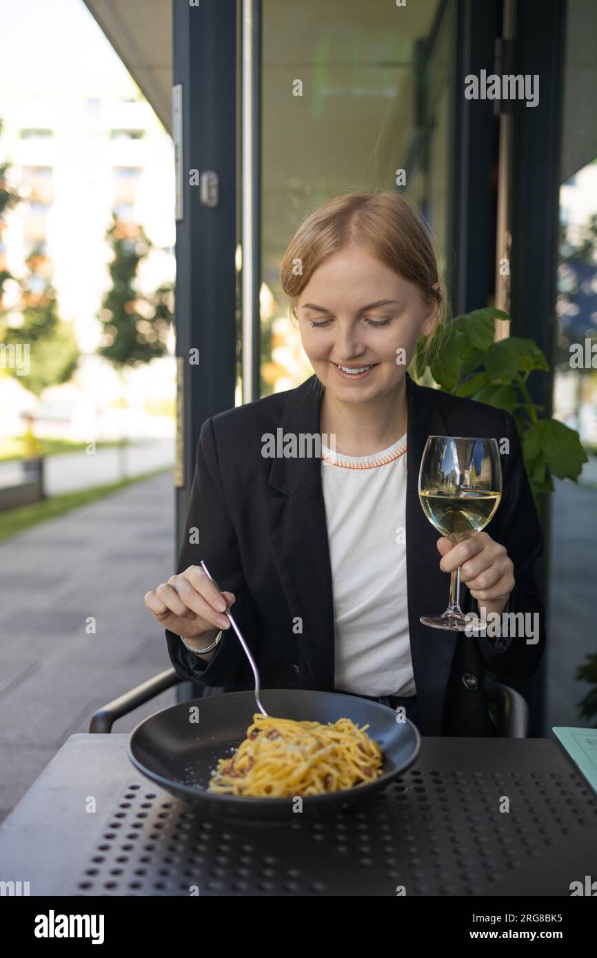 Portrait of a smiling blonde woman eating Italian pasta carbonara and ...