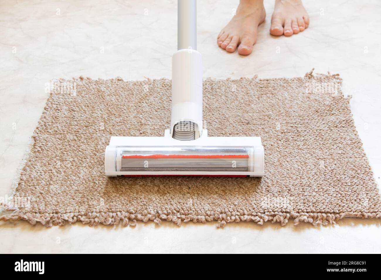 Vacuum cleaning on a beige rug on the floor and next to woman's leg ...