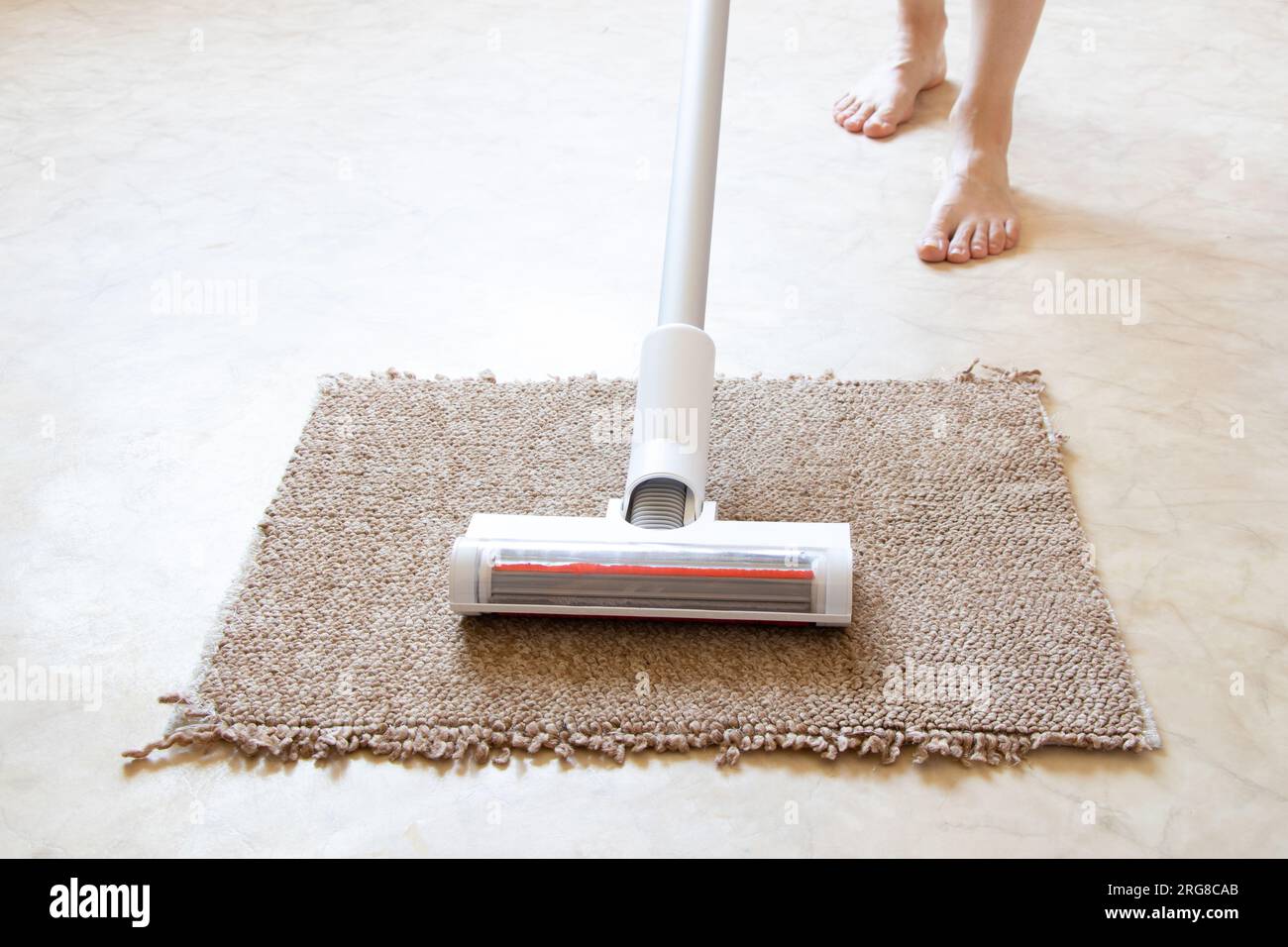 Vacuum cleaning on a beige rug on the floor and next to woman's leg ...