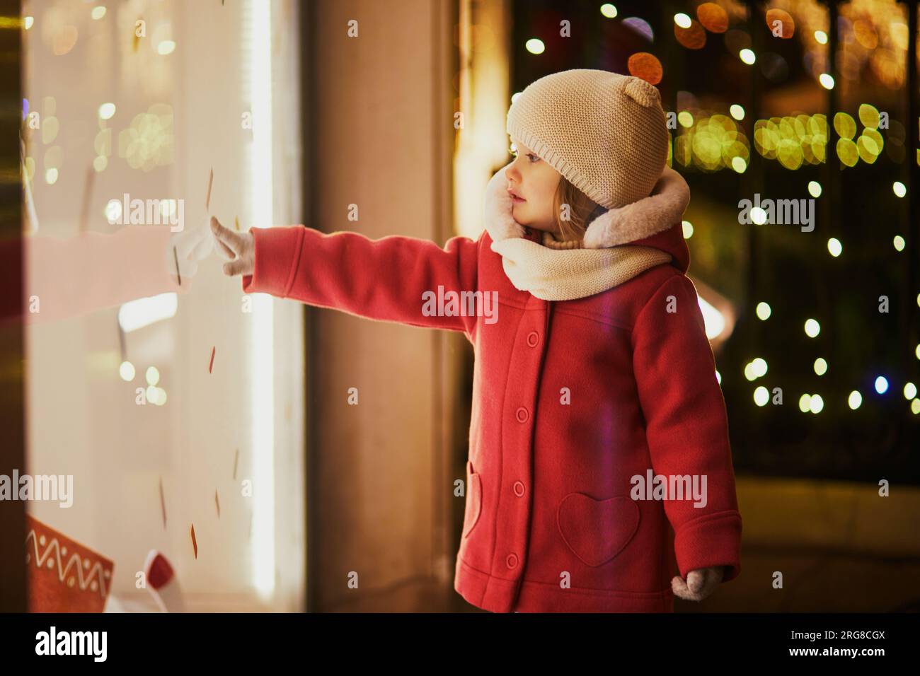 Toddler girl looking at window glass of large department store ...