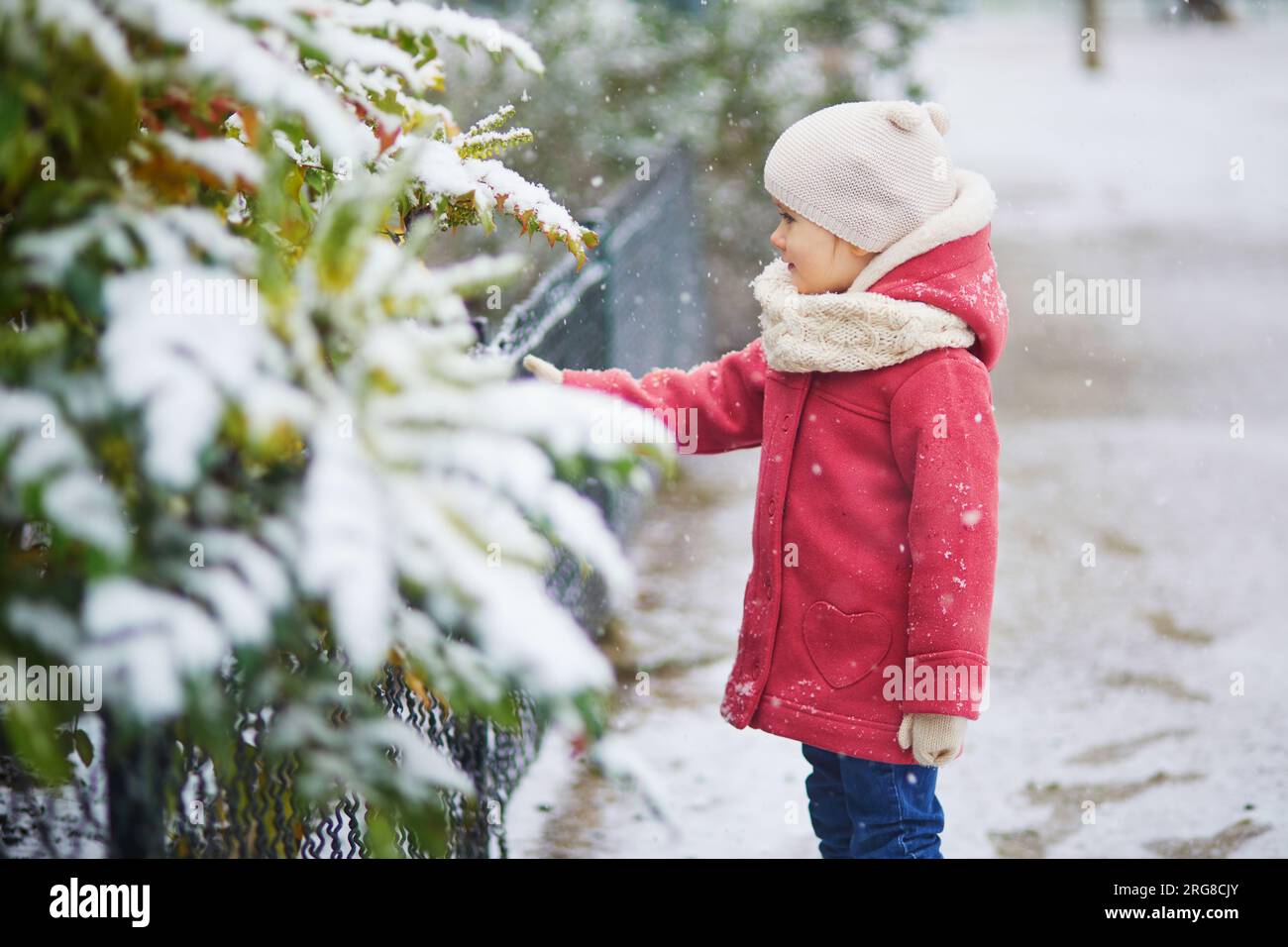 Adorable toddler girl on a day with heavy snowfall. Happy child playing ...