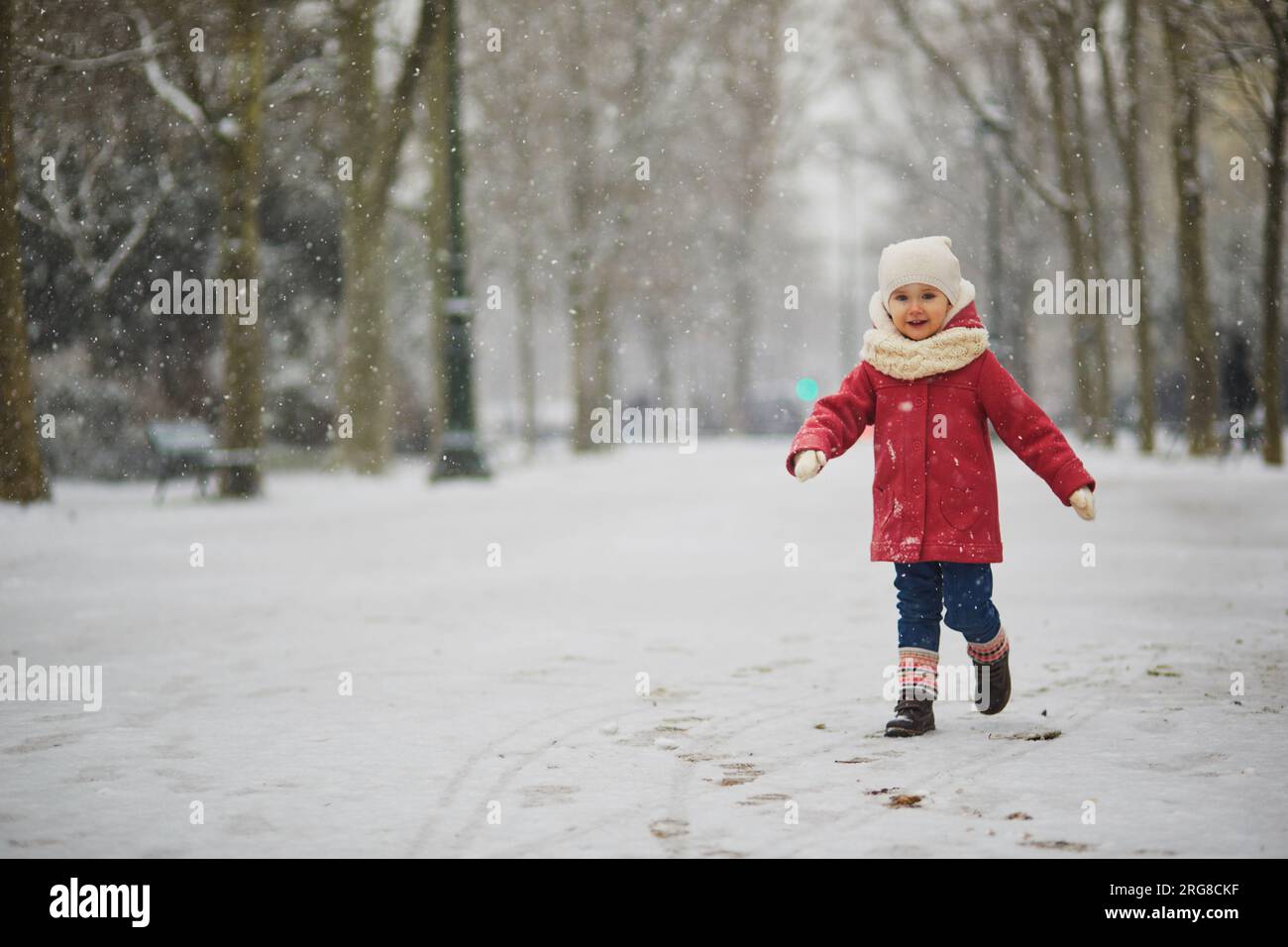 Adorable toddler girl on a day with heavy snowfall. Happy child playing ...